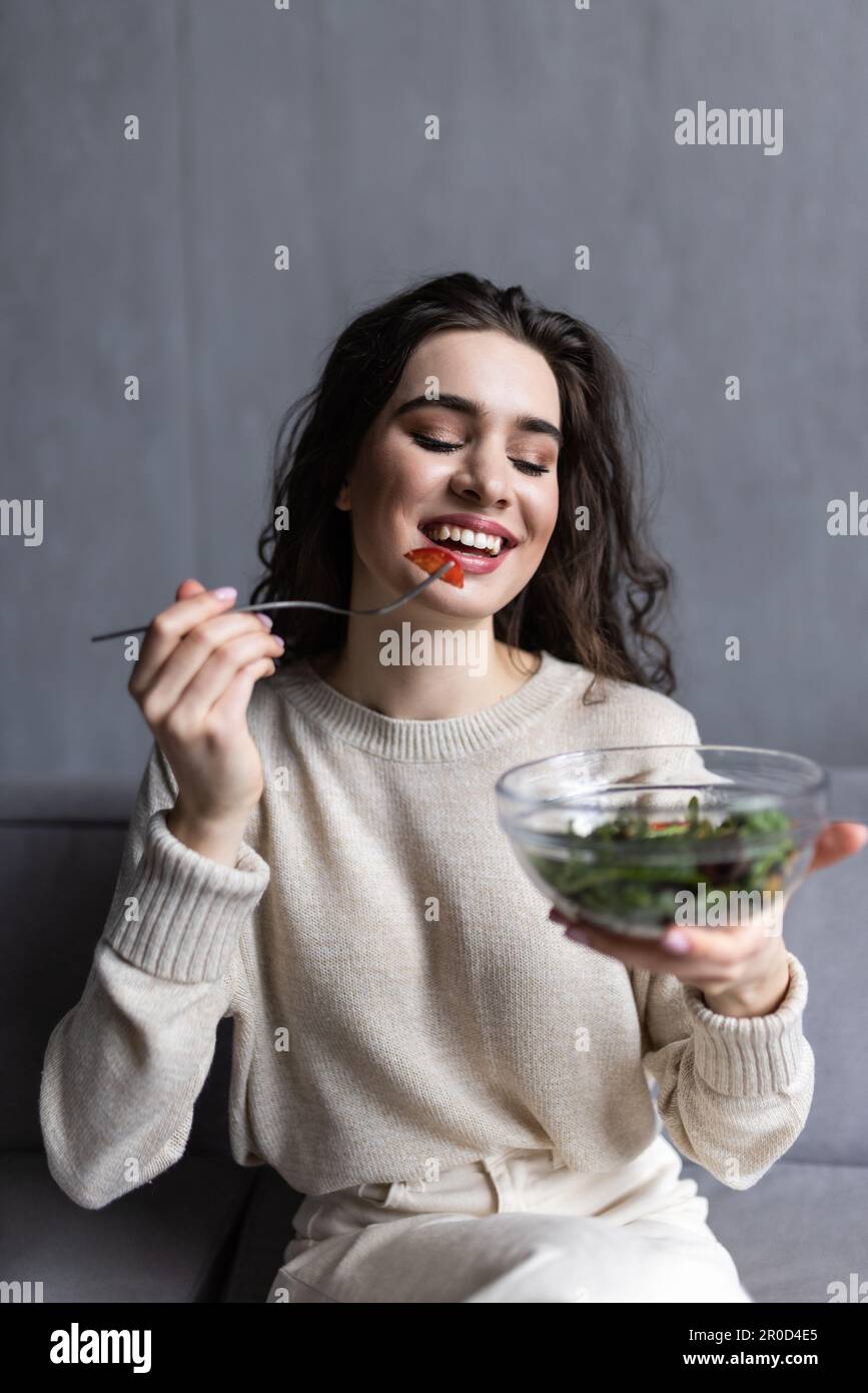 Happy woman relaxing on the sofa eating salad in her living room Stock ...
