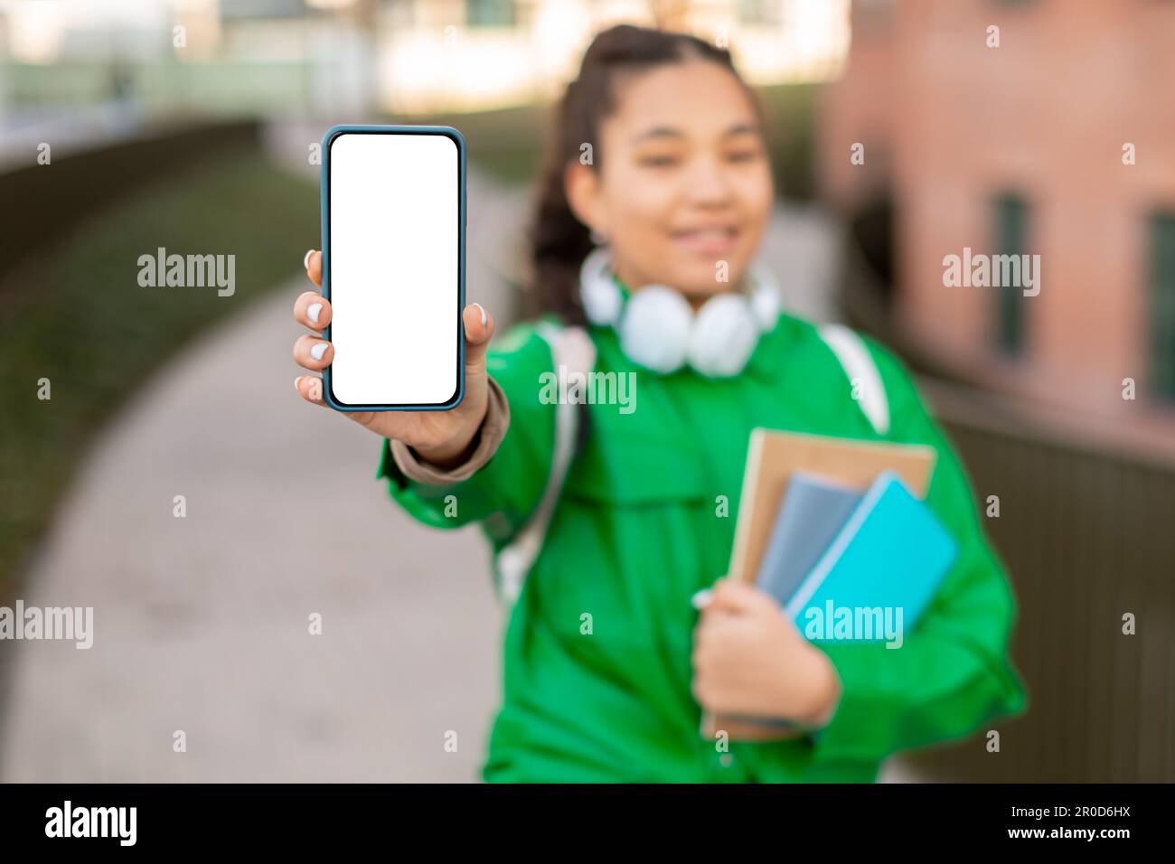 Teen student girl demonstrating blank smartphone, posing at college ...