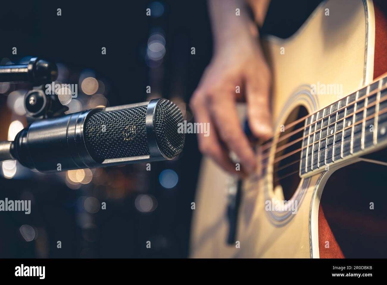 Male musician playing acoustic guitar behind microphone in recording ...
