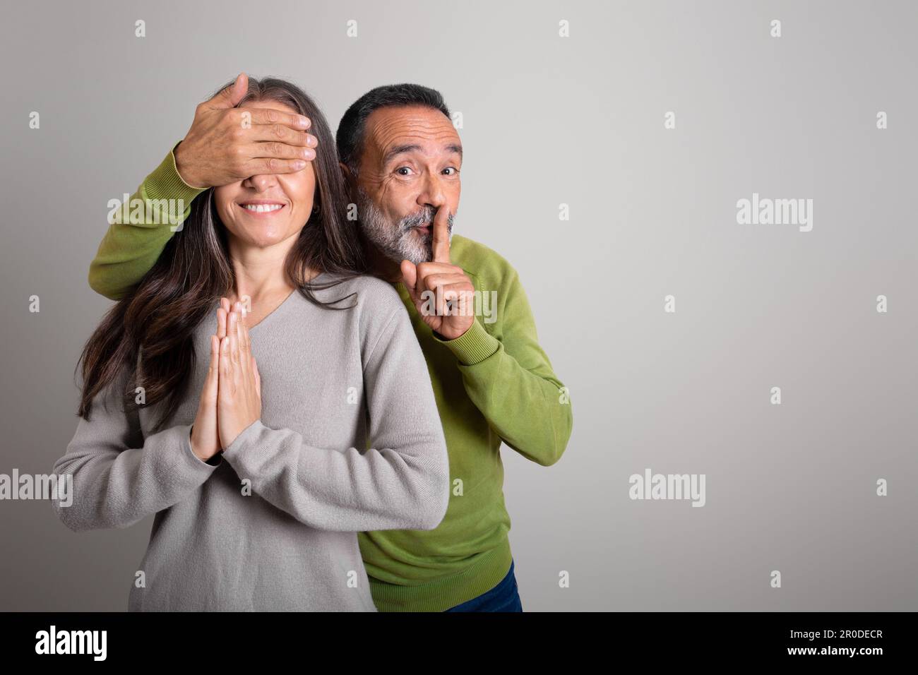 Smiling caucasian elderly man closes eyes to wife, makes shh gesture on ...