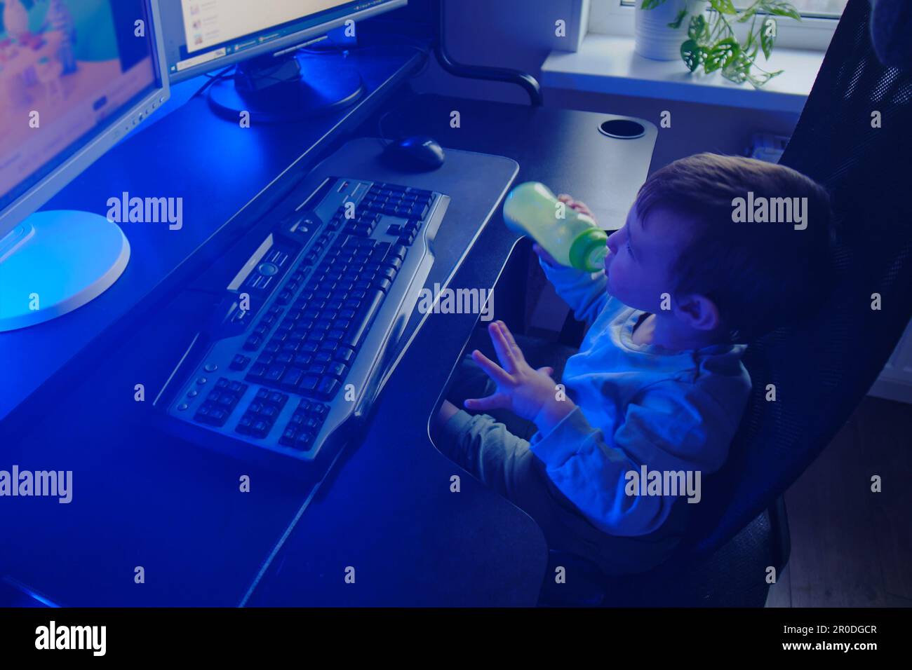 Happy baby is sitting at the computer keyboard with a bottle of milk in ...