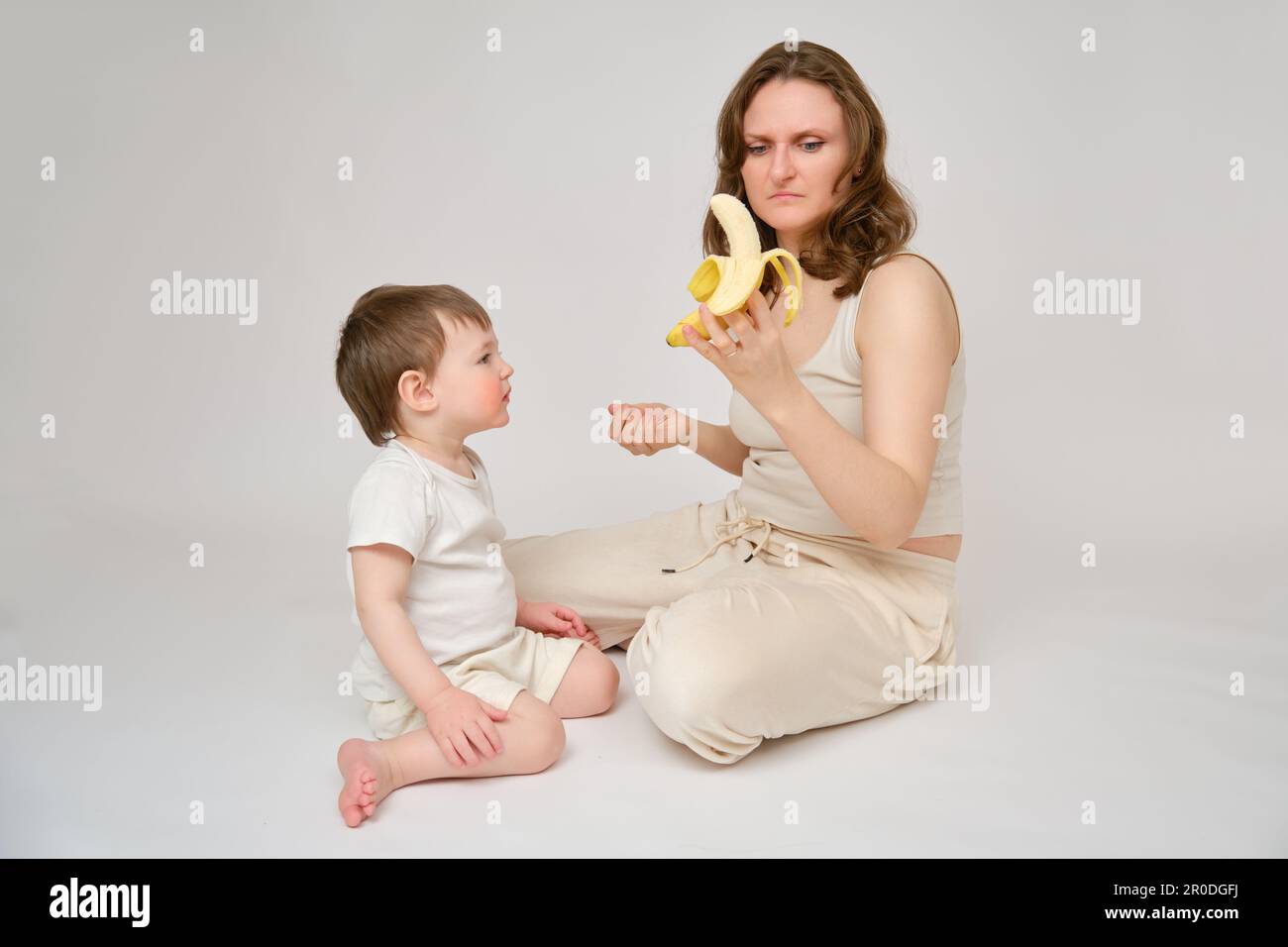 Happy baby with mother eating banana on studio white background ...