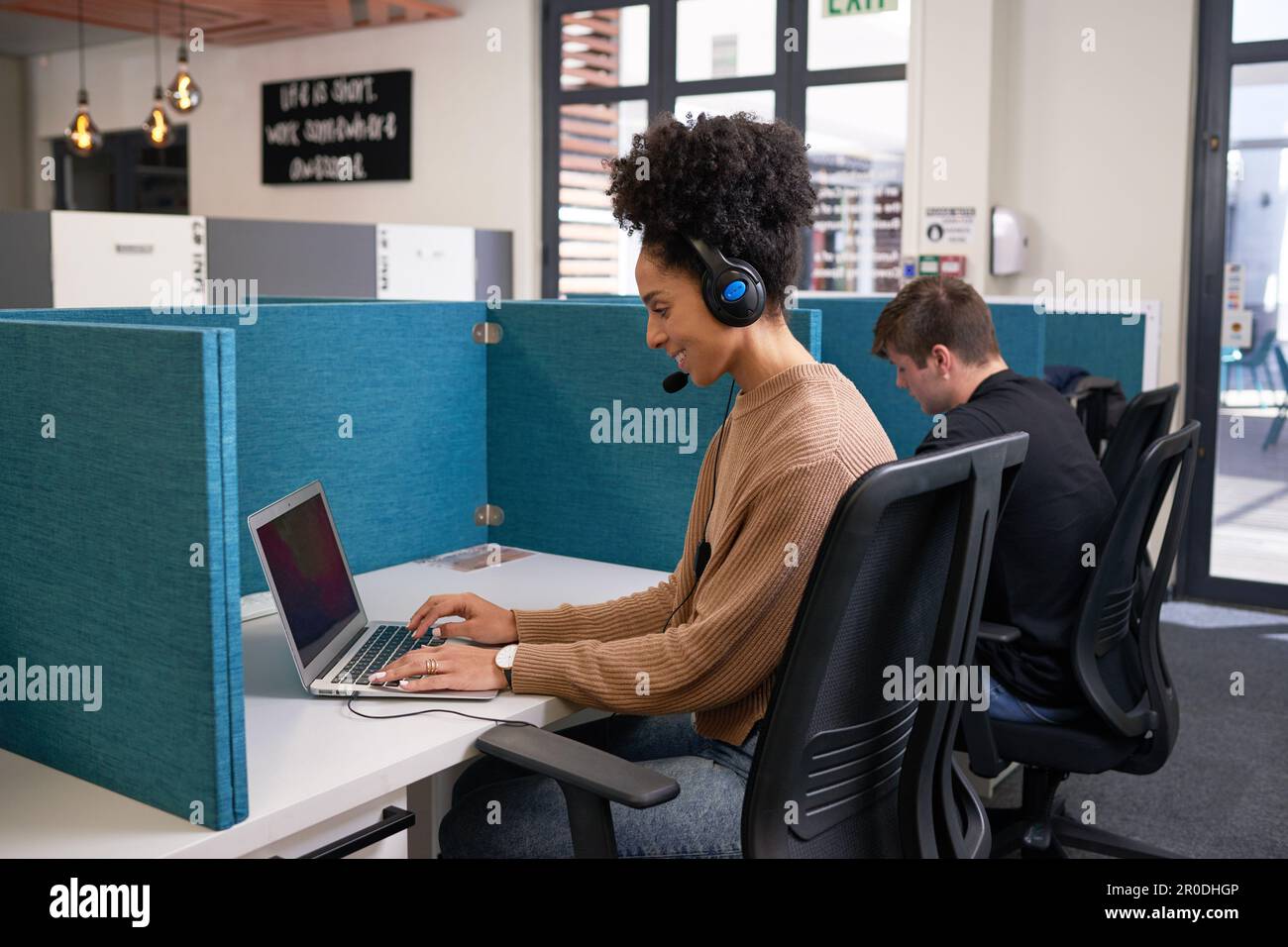 Two young people work side by side in office with desk dividers ...
