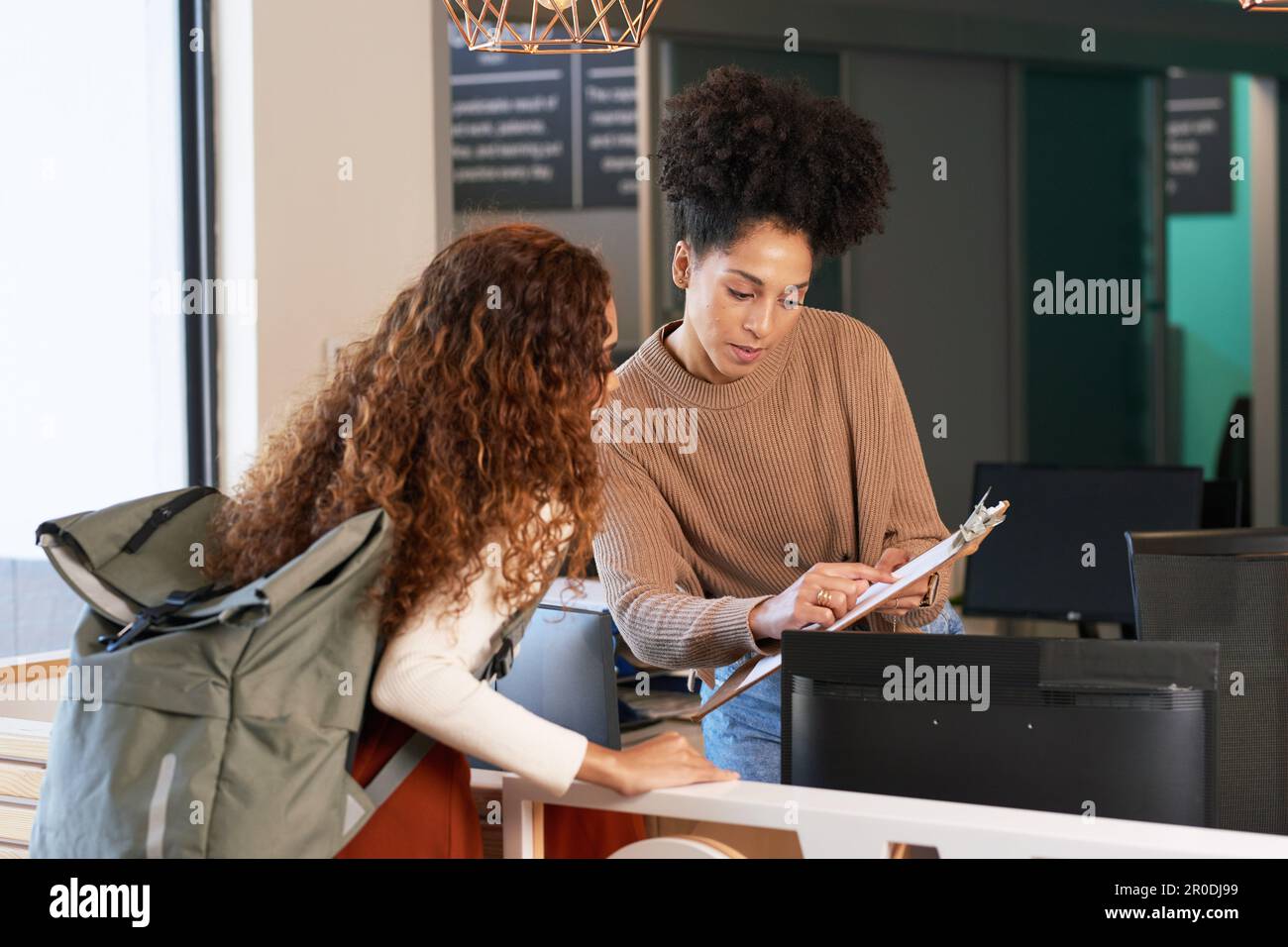 Young woman checks in at front desk, reception, hotel, college library ...