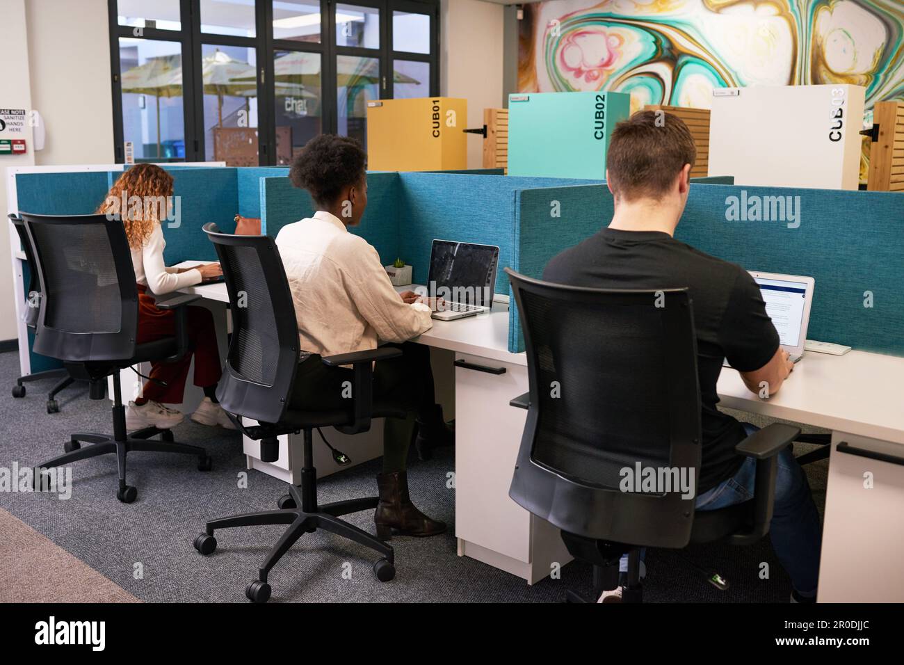 Three young people share coworking space, work side by side with desk ...