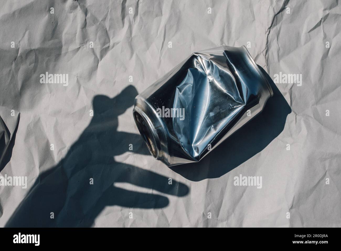 A crumpled paper with a hand shadow and crumbled crushed aluminum can ...