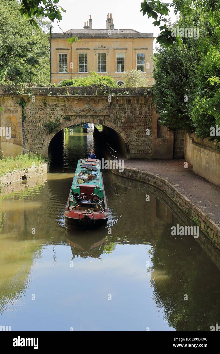 A green and red canal boat passing under a bridge in Sydney Gardens ...