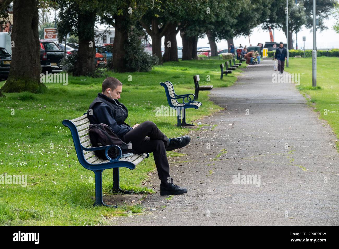 A young man sitting on a park bench alone listening to music on his ...