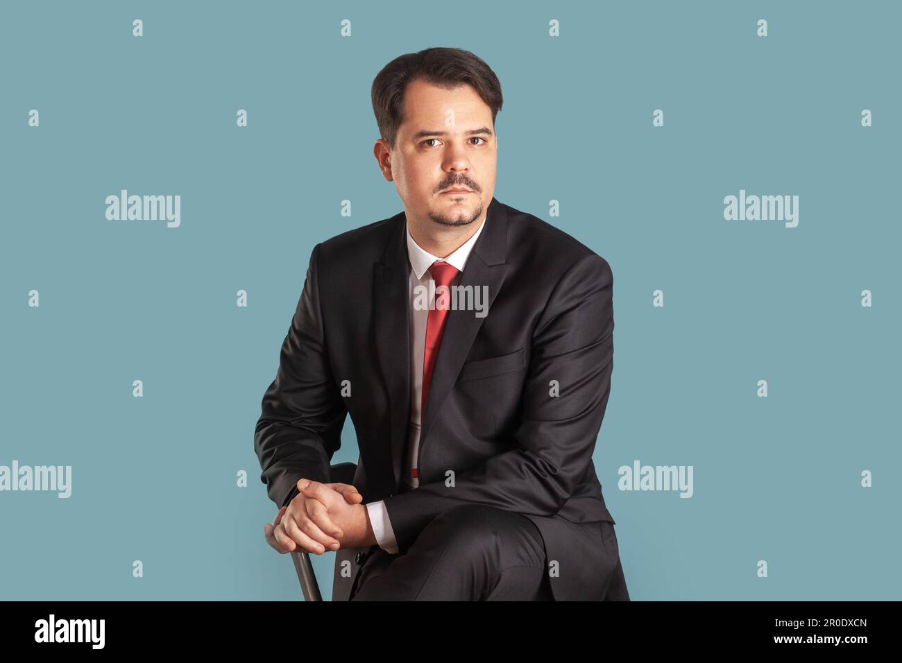 Portrait of handsome serious strict man with mustache sitting on chair ...
