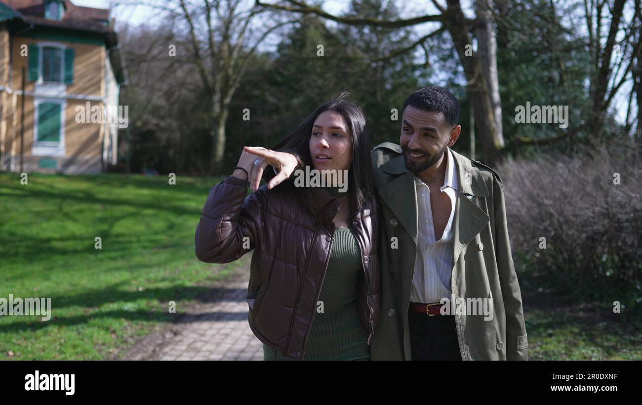 Happy couple pointing at distance saying hello to friend while walking ...