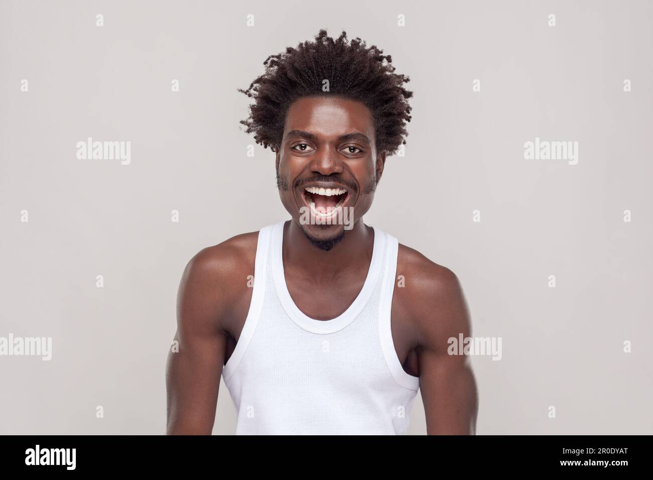 Emotional gorgeous man with Afro hairstyle grinning broadly, enjoying ...