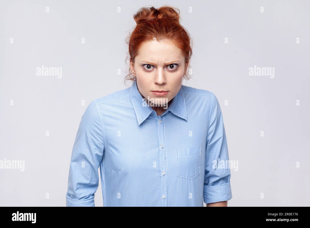 Portrait of angry aggressive ginger woman wearing blue shirt looking at ...