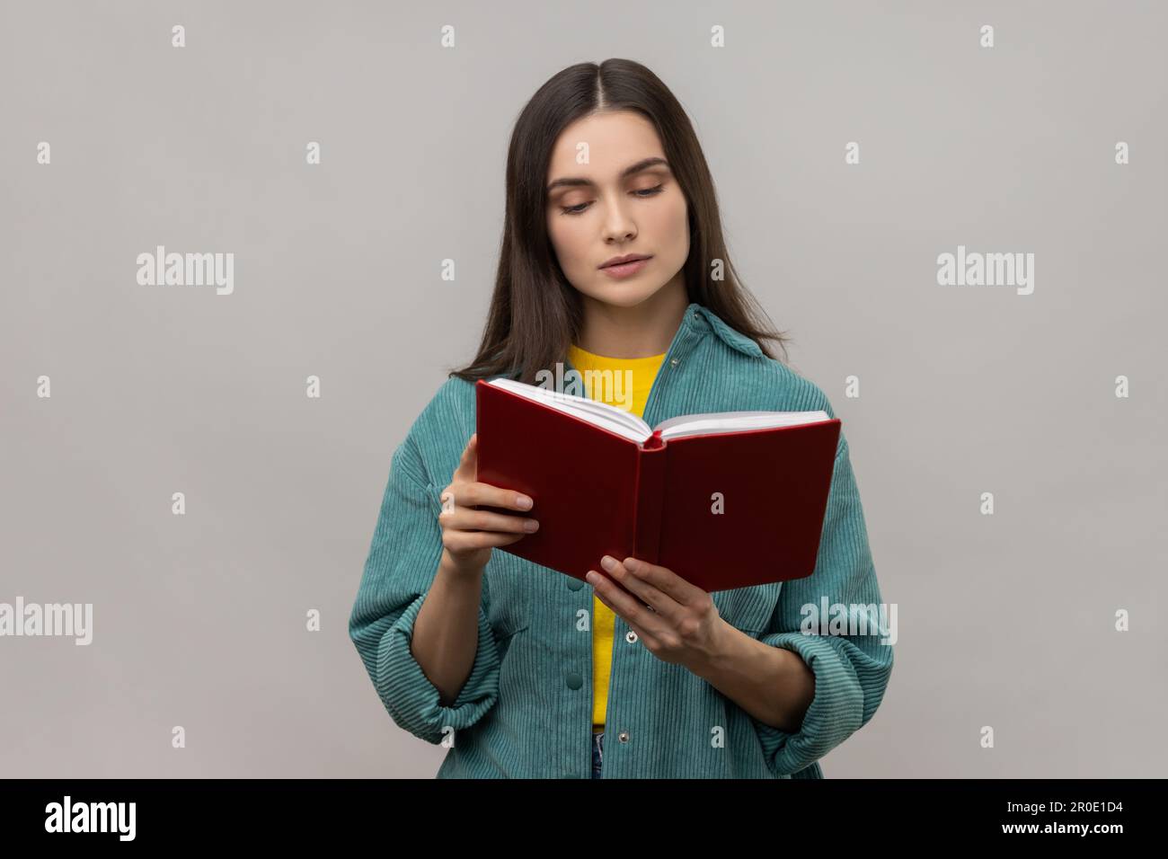 Portrait of serious concentrated woman with dark hair reading book with ...