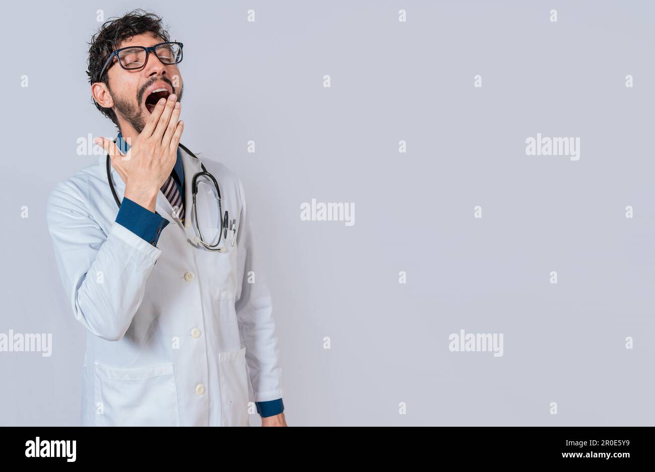 Young sleepy doctor yawning on isolated background. Tired of working ...