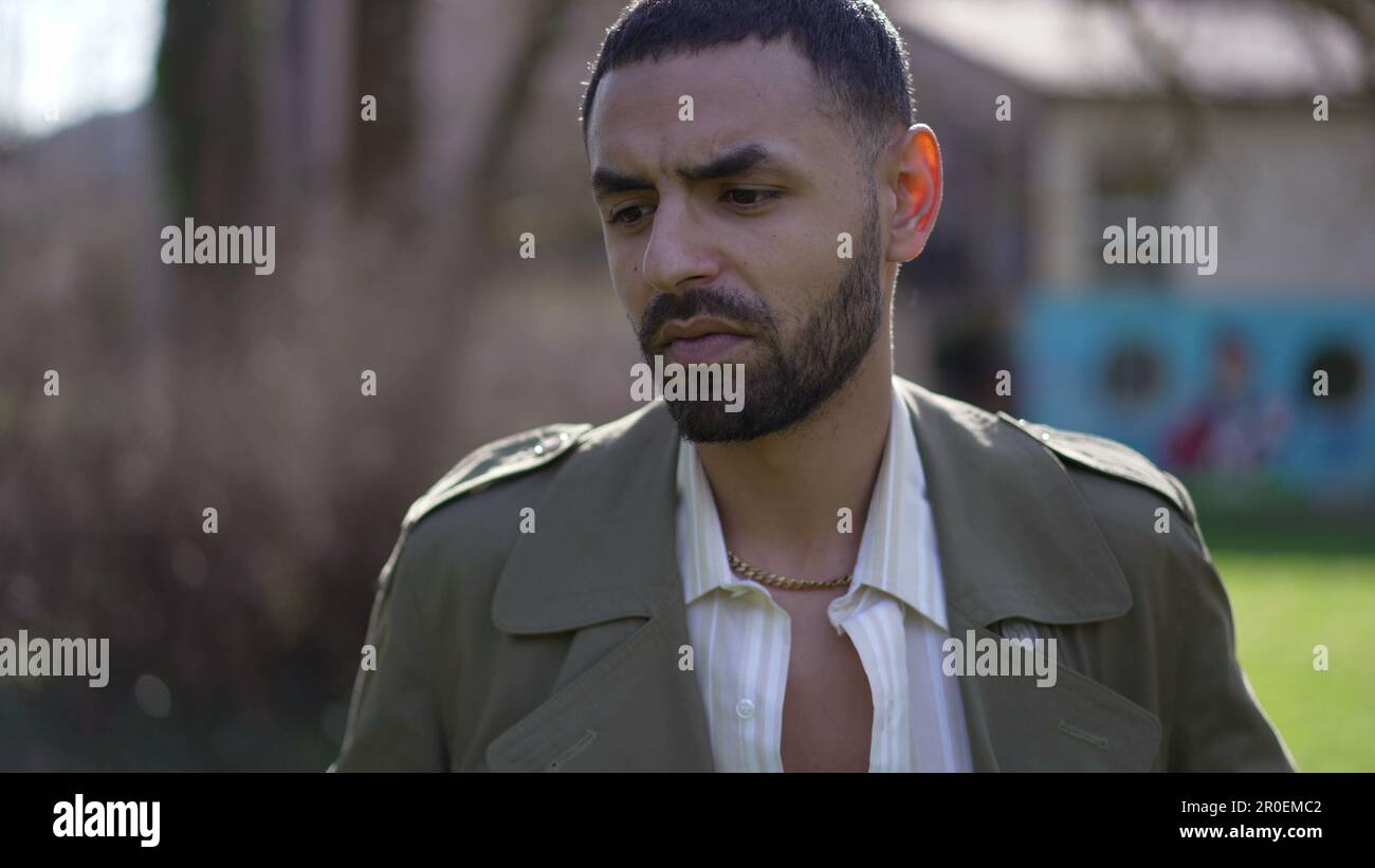 One thoughtful young Middle Eastern man standing outside at park ...