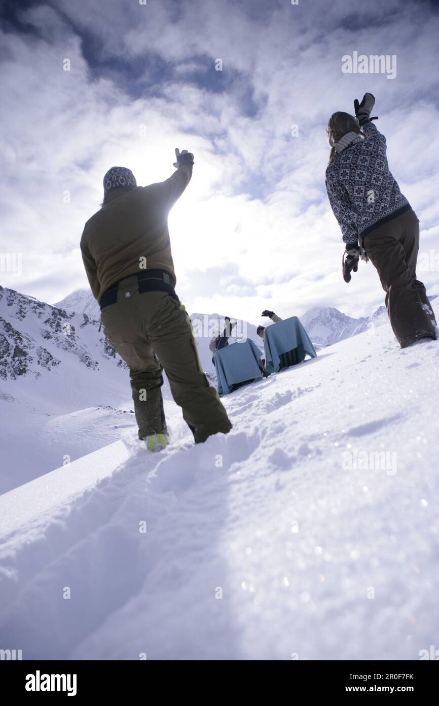 Two young people relaxing on lounge chairs, two others wave to them ...