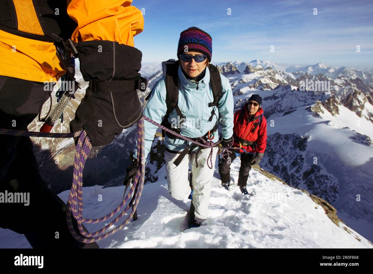 A woman and a man on the rope of a guide climb an exposed snowy ...