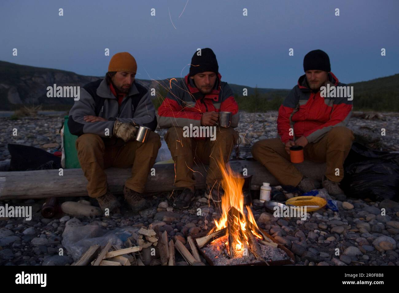 Three men sitting around a campfire at dusk, South Nahanni River ...