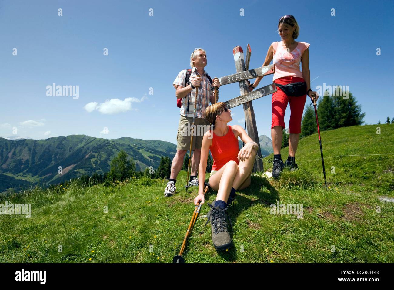 Three hikers resting at sign post, Bichlalm (1731 m), Grossarl Valley ...