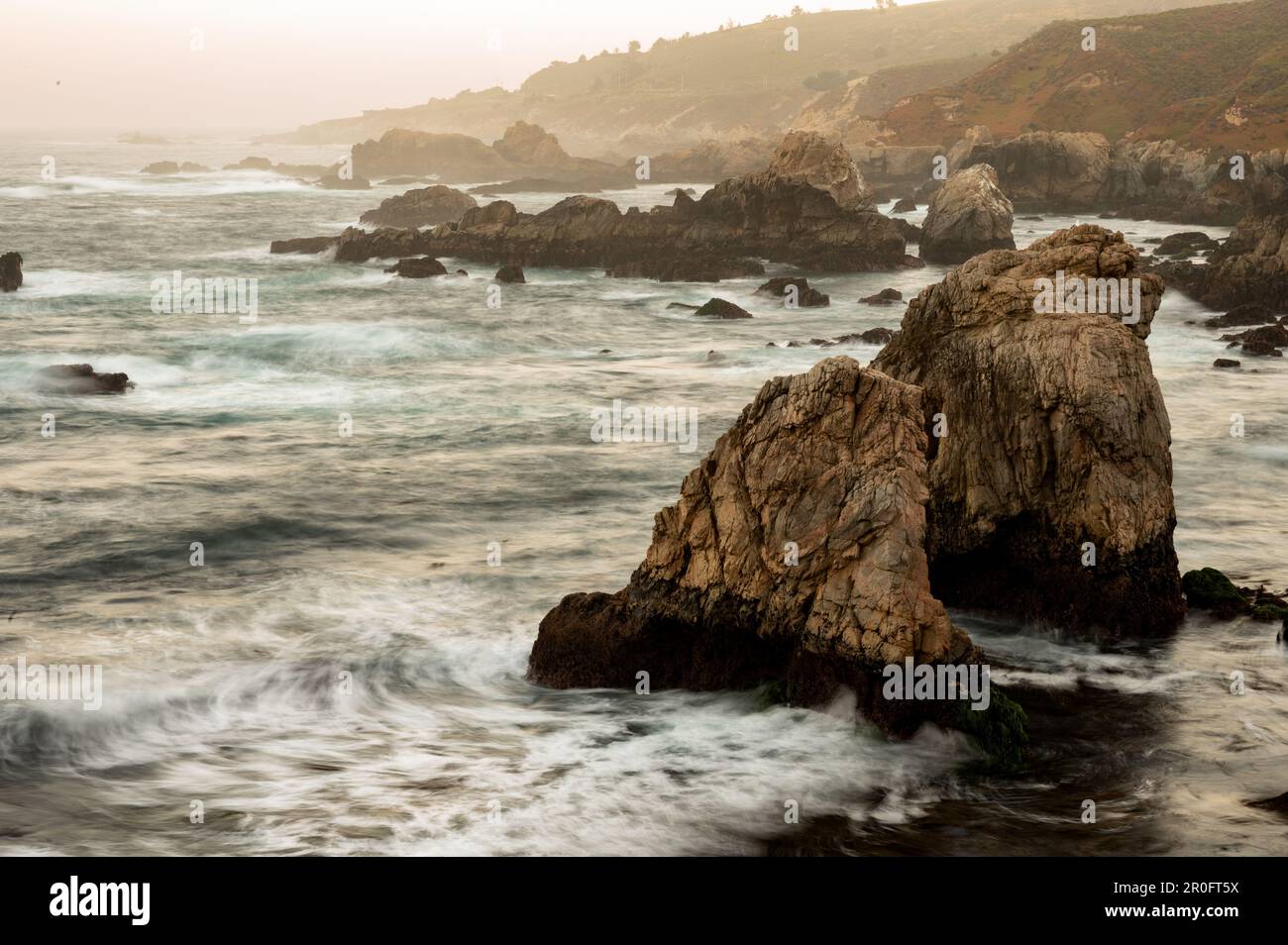 An oceanside shoreline with rocks in water at sunset Stock Photo - Alamy