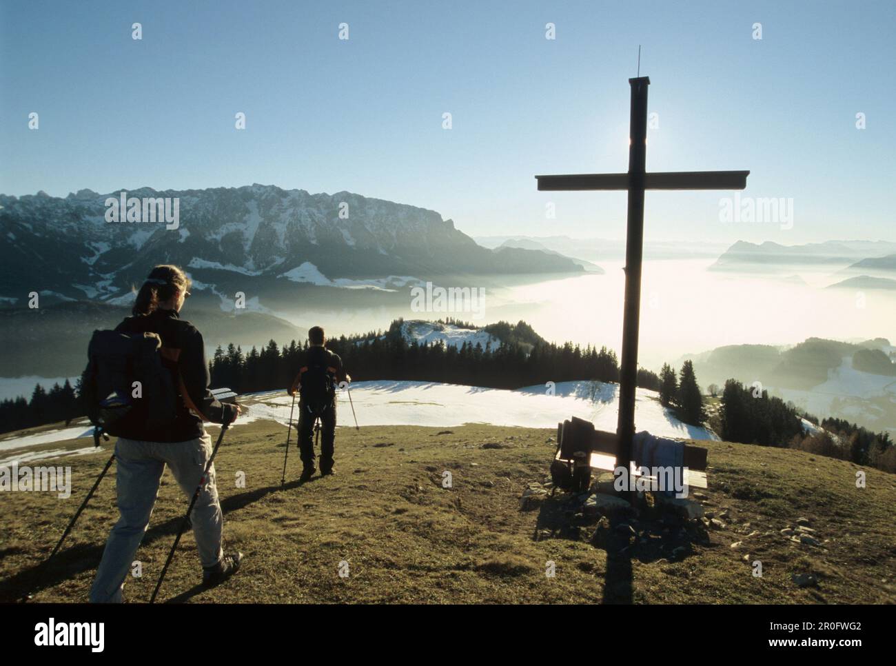 Two hikers at summit cross, view into valley of Inn river, Bavaria ...