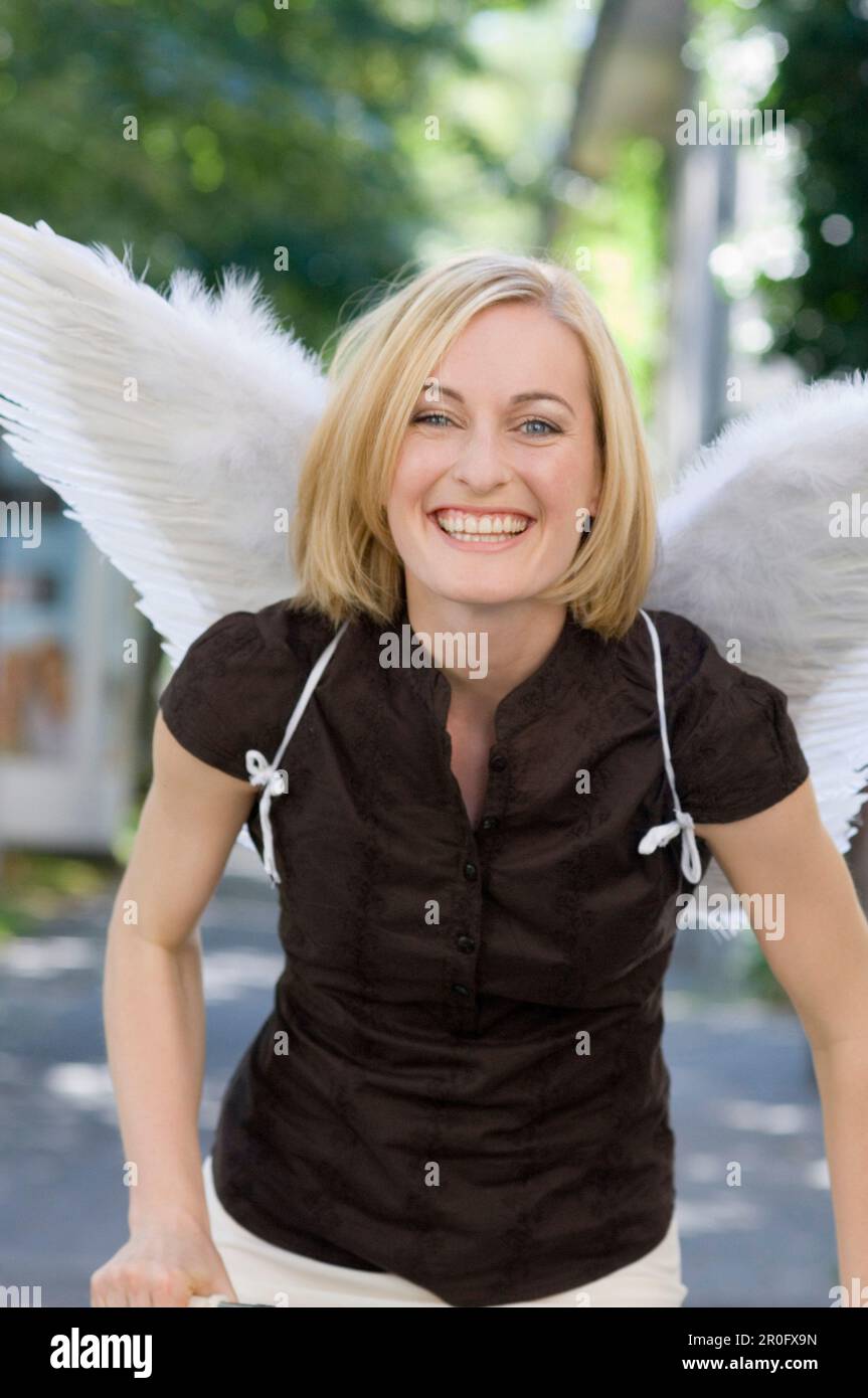 Mid adult woman wearing angel wings riding a bicycle Stock Photo - Alamy