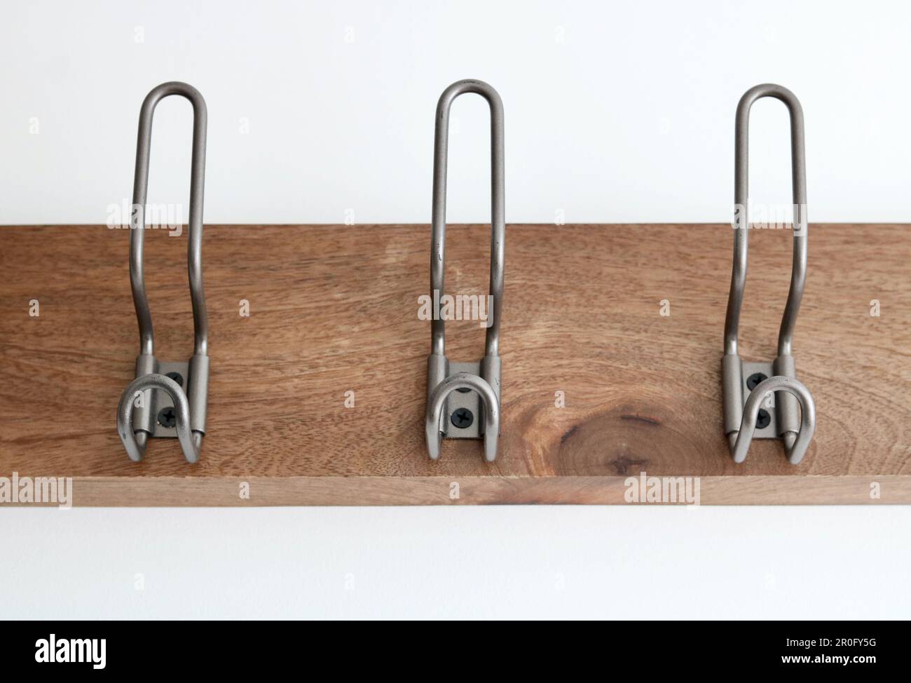 Three metal coat hooks on wooden panel attached to white wall Stock ...
