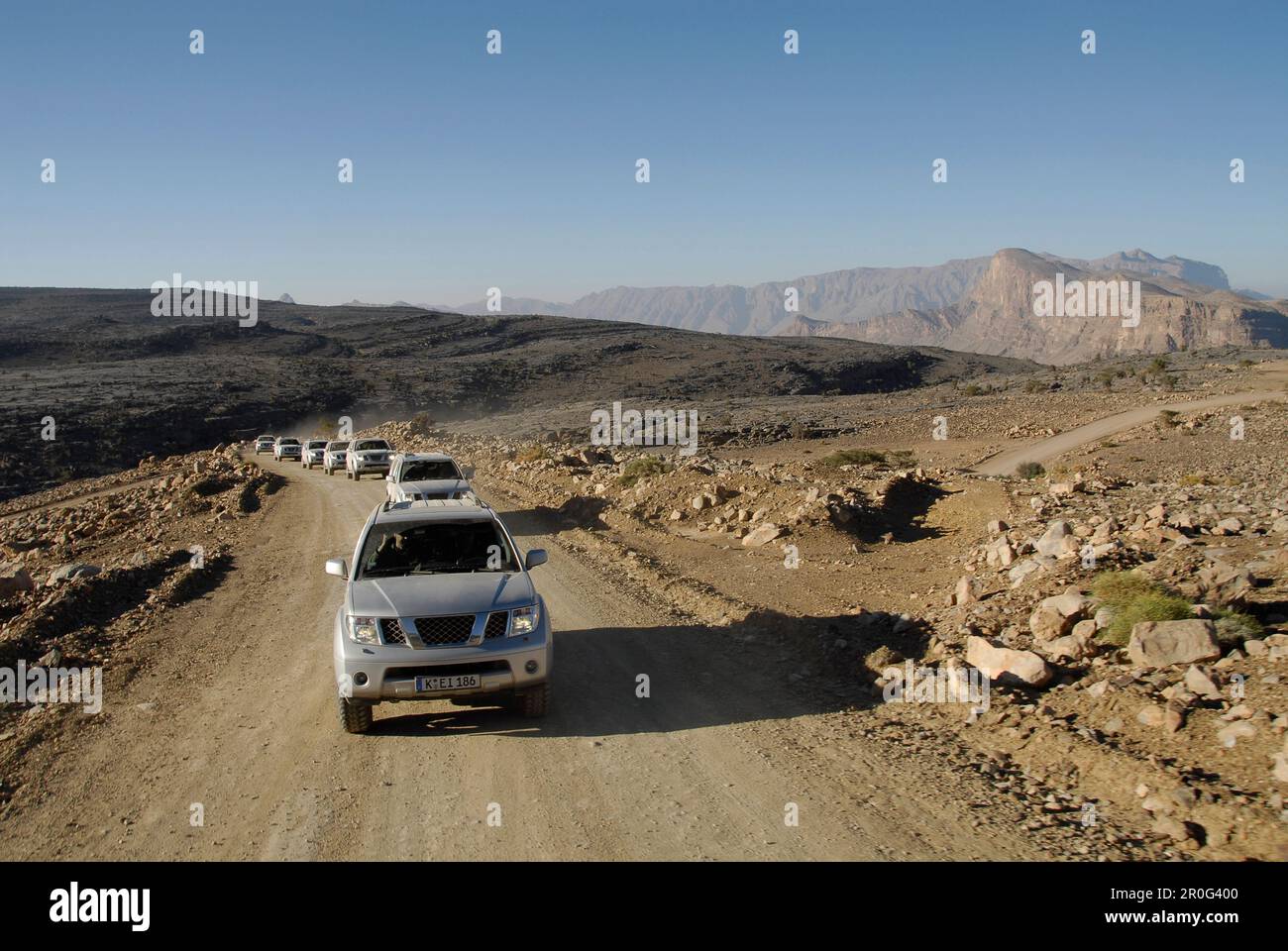 A row of all-terrain vehicles driving on a road through barren scenery ...