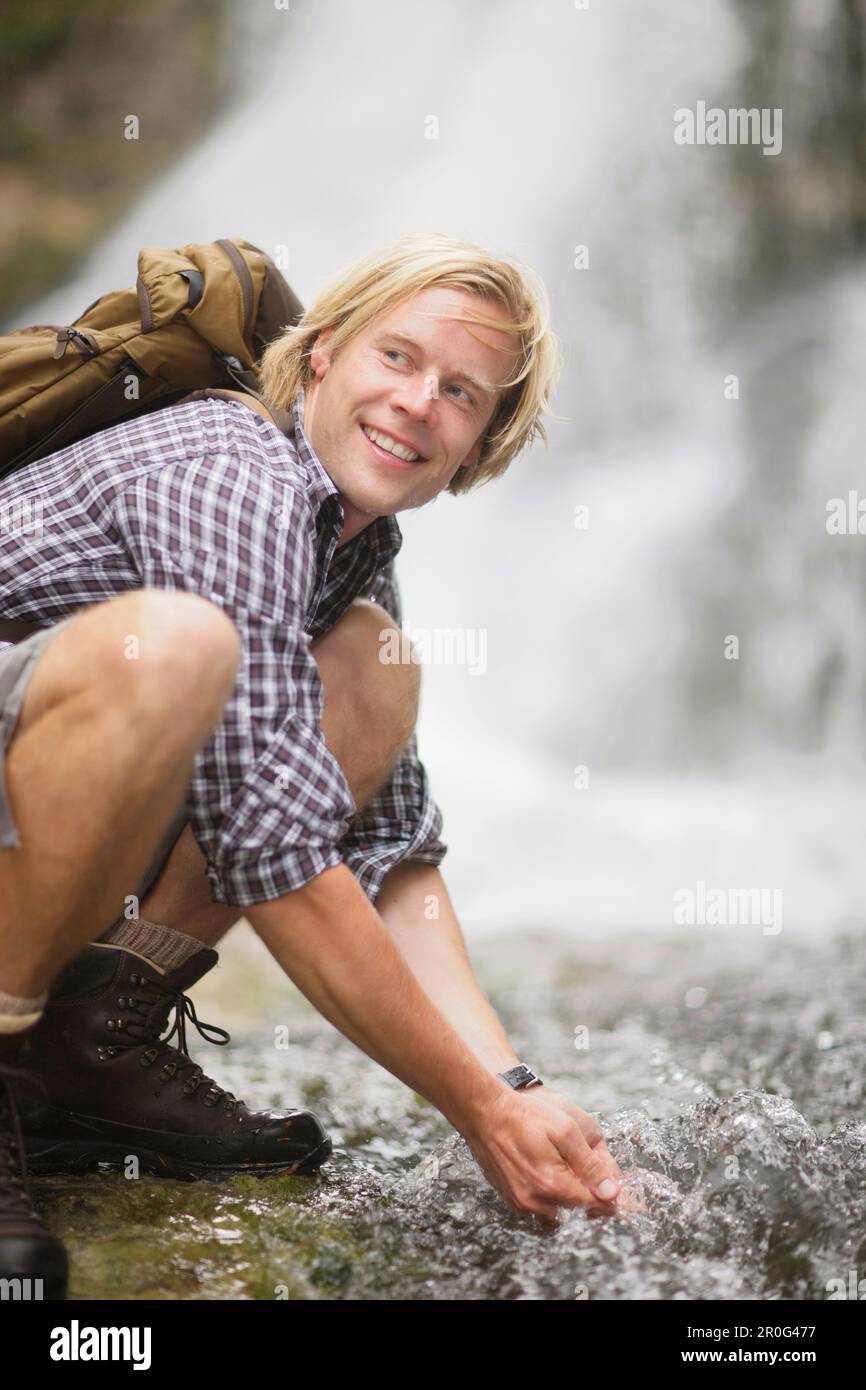 Young man drinking from waterfall, Werdenfelser Land, Bavaria, Germany ...