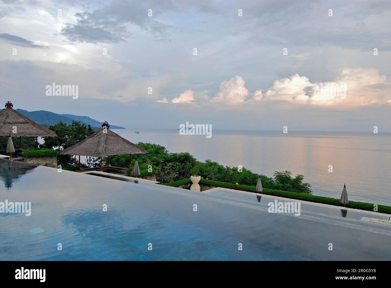 The deserted infinity pool at the Amankila Resort under clouded sky ...