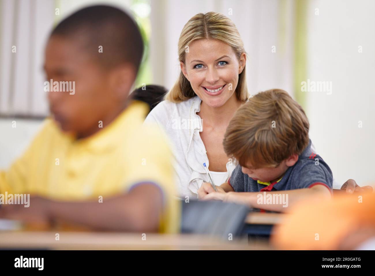 Shes a dedicated educator. A smiling teacher sitting the classroom with ...