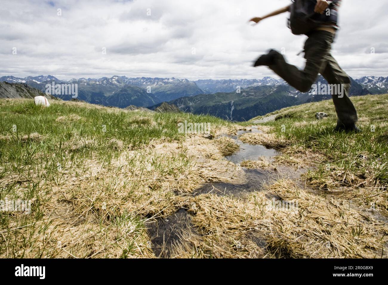 Woman jumping over a stream, Sarotla Joch, Montafon, Vorarlberg ...
