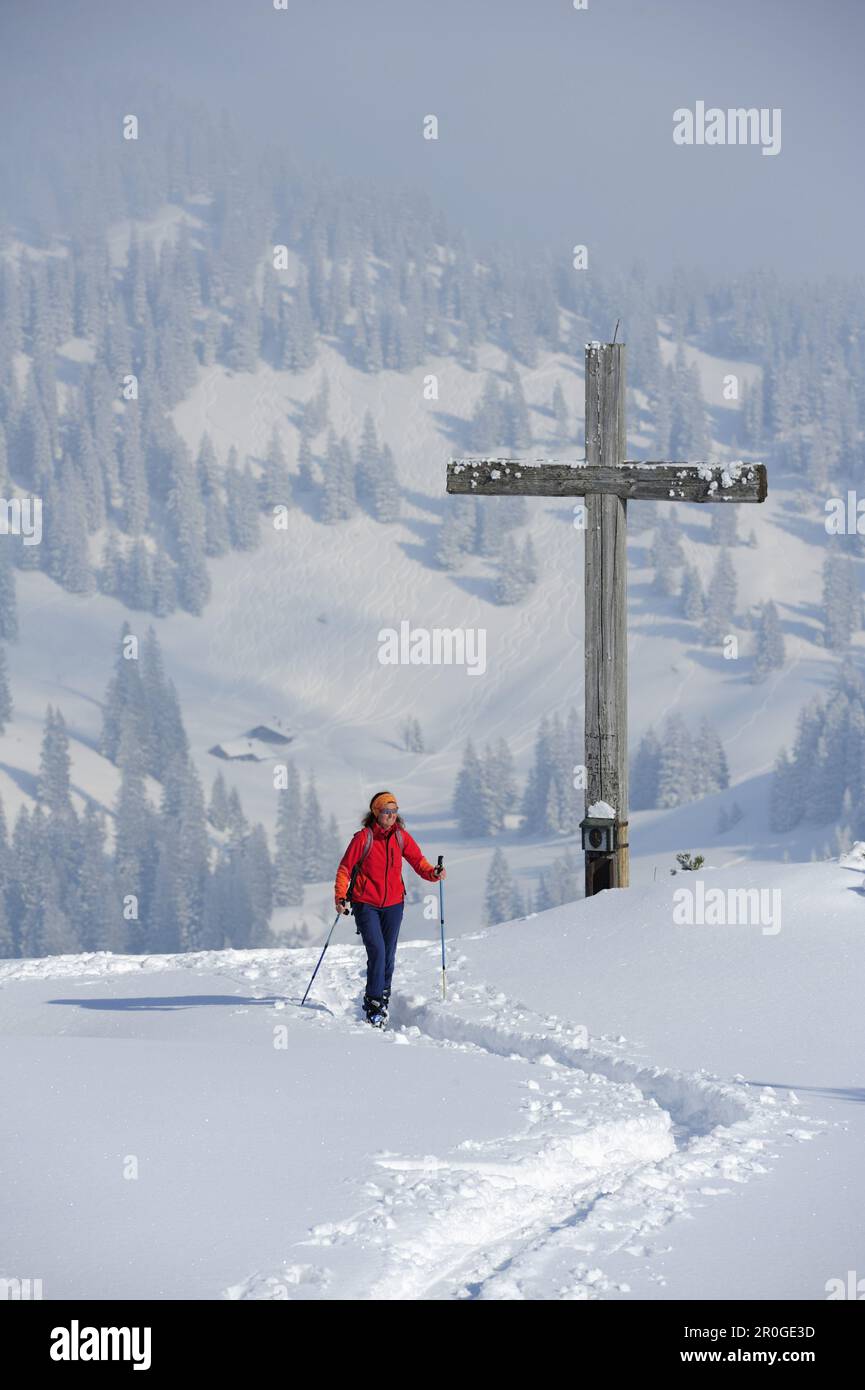 Woman backcountry skiing ascending in a track in front of summit cross ...