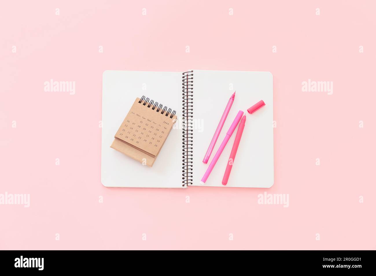 Flip paper calendar for June with notebook and pens on pink background ...