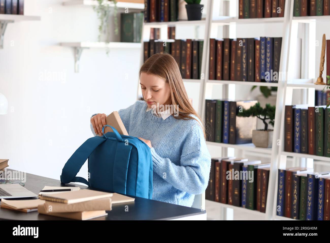 Female student putting book into backpack in library Stock Photo - Alamy