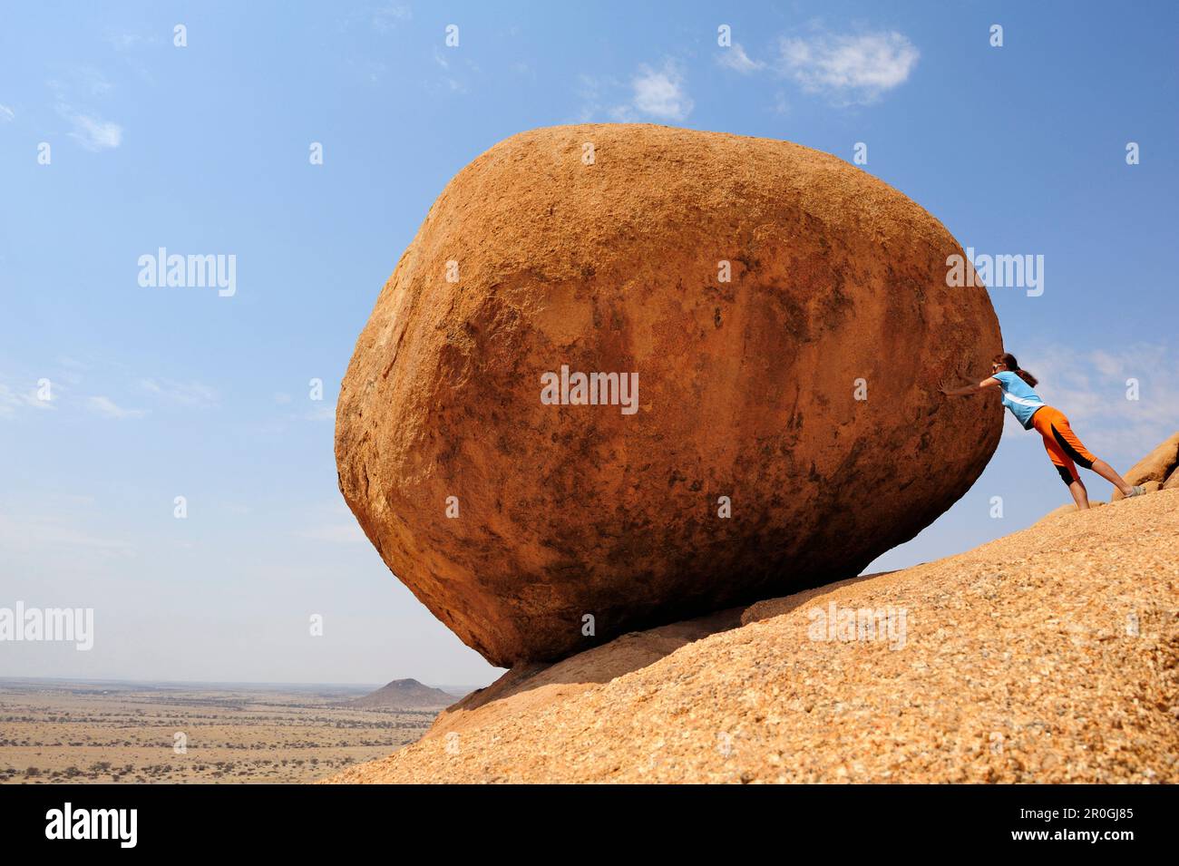Woman pushing red balancing granite rock from slab, Great Spitzkoppe ...