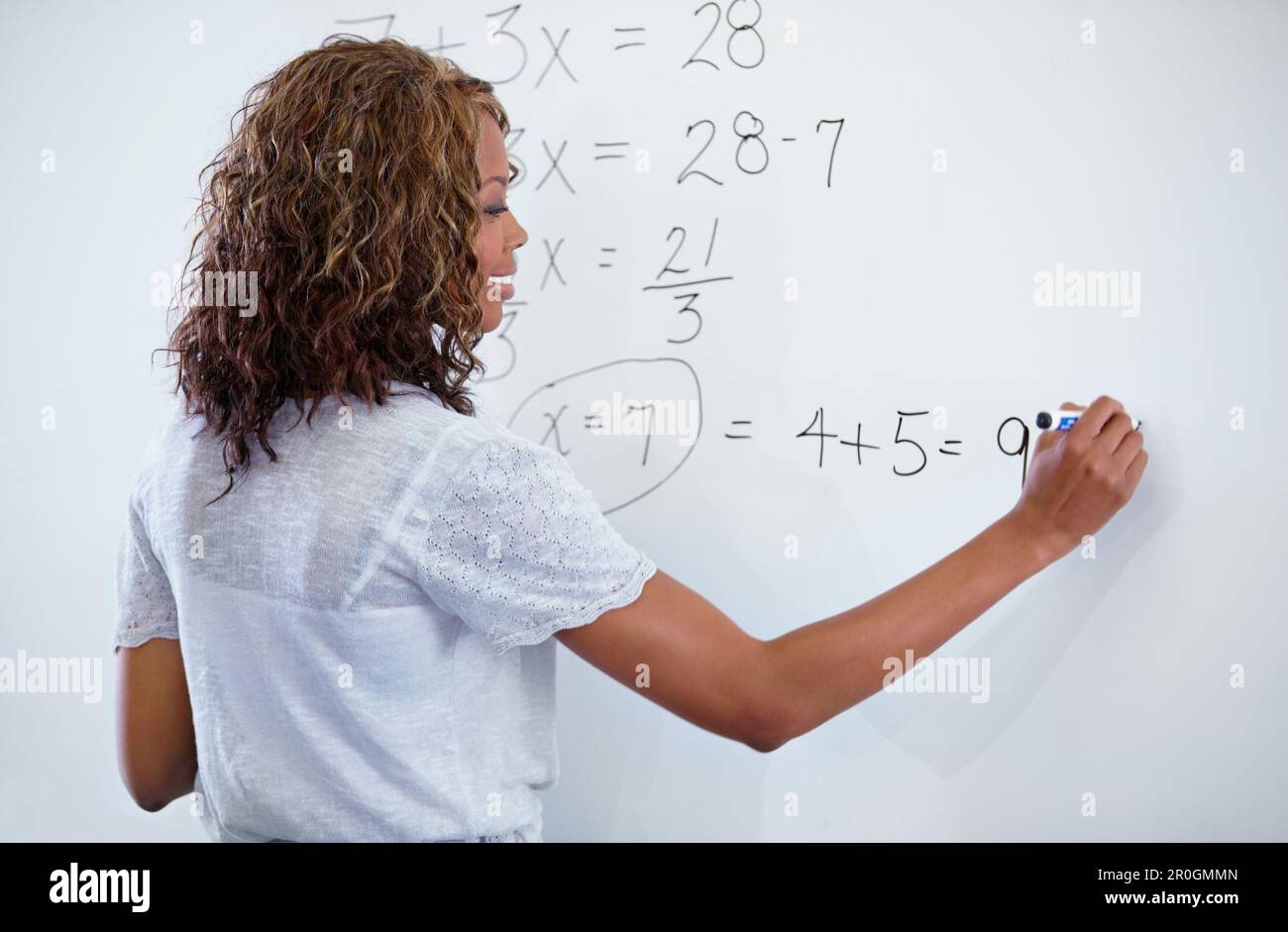 Teaching maths. A young teacher doing maths equations on the whiteboard ...