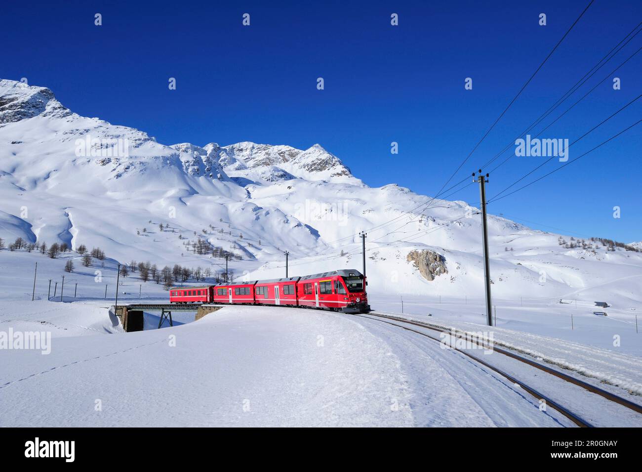 Train of Rhaetien railway driving over bridge through winter landscape ...