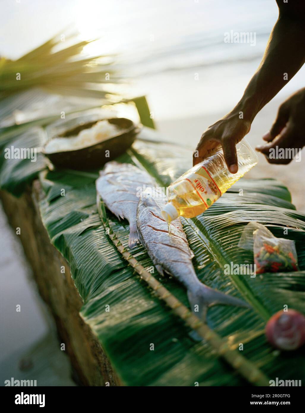 Man preparing Creole fish barbecue on the beach, in the background ...