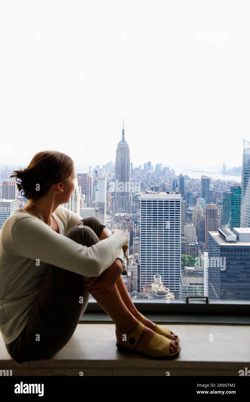 Woman sitting on a window sill while looking at Empire State Building ...