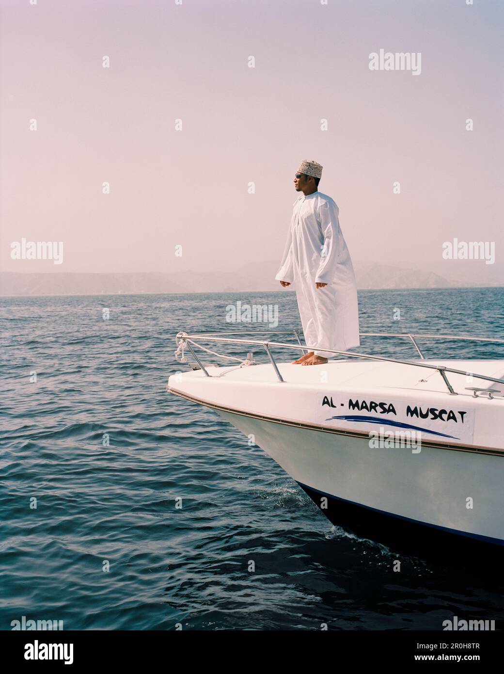 OMAN, Muscat, man standing on deck of boat in traditional clothing at ...
