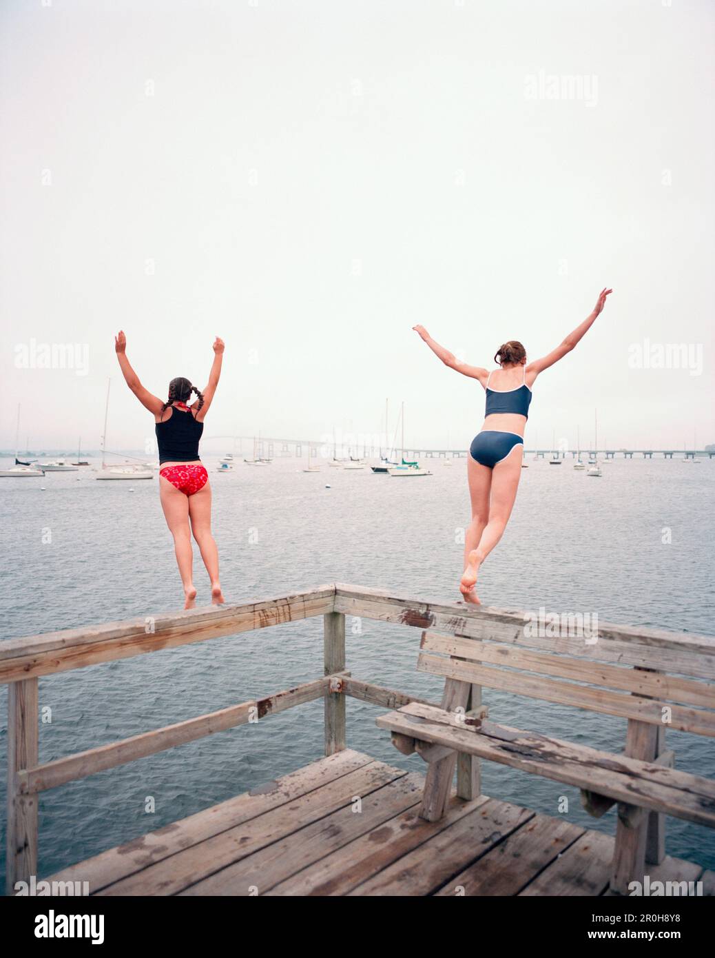 USA, Rhode island, rear view of women jumping off the pier into water ...