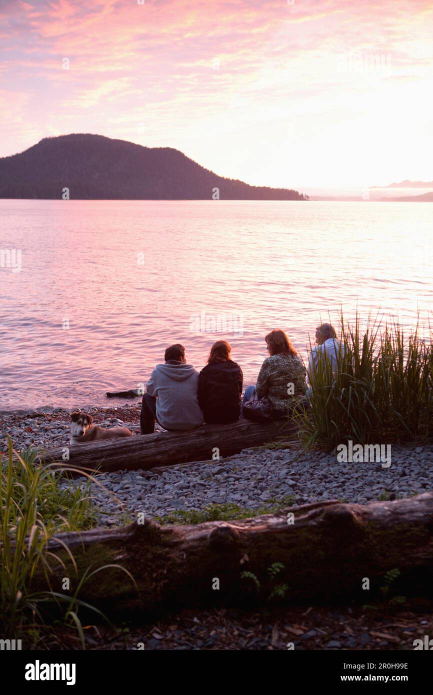 ALASKA, Sitka, people enjoy the sunset and sit on a log at Halibut Cove ...