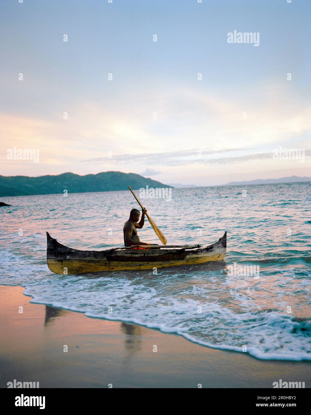MADAGASCAR, man in dugout canoe at dusk, Jardin Vanille Beach, Nosy Be ...