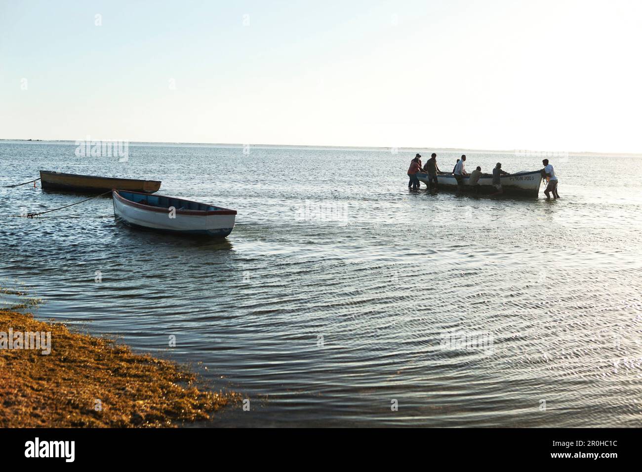 MAURITIUS, fishermen pull their boat through shallow water and closer ...