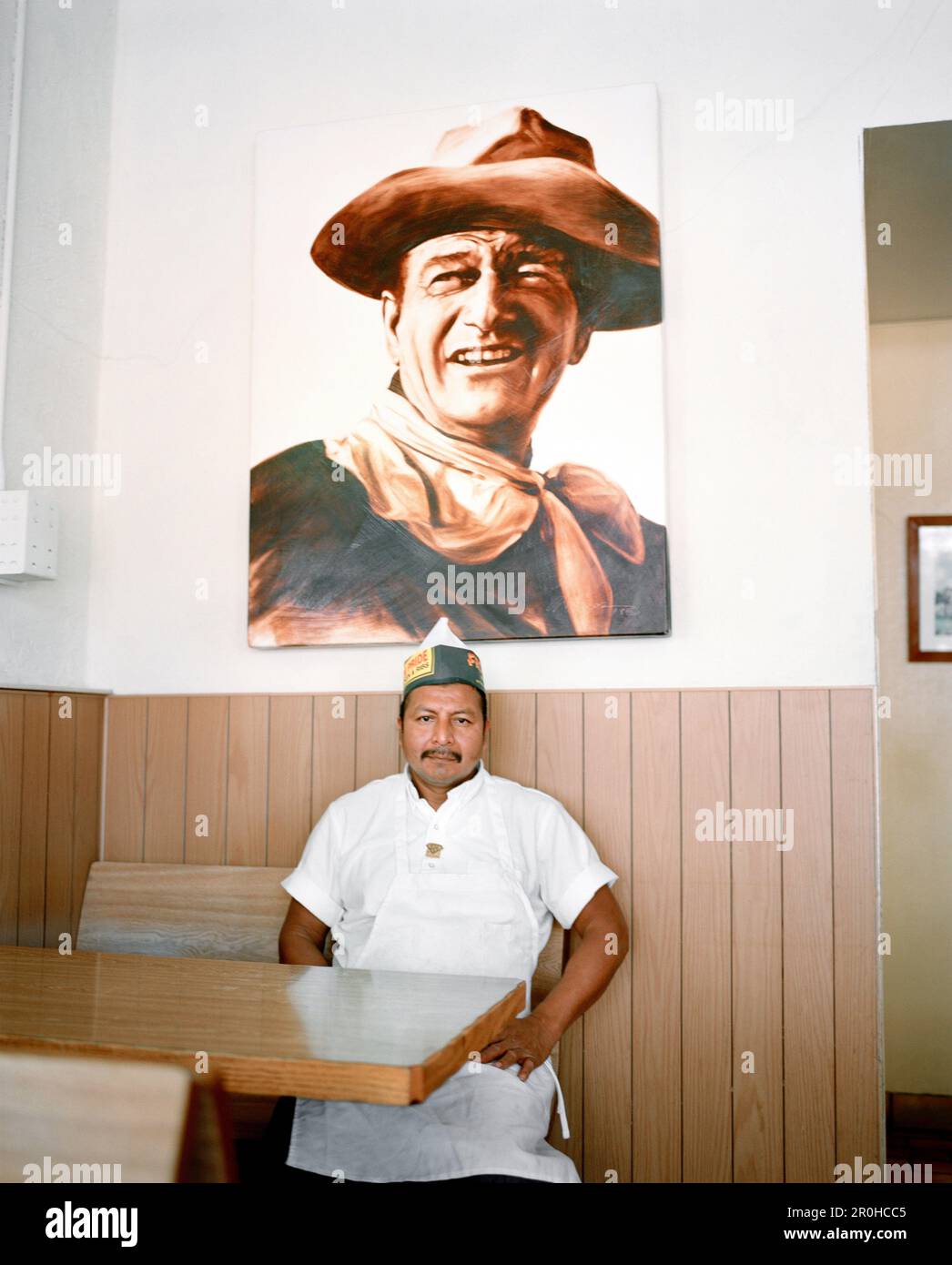 USA, New Mexico, cook sitting under John Wayne painting, Frontier ...