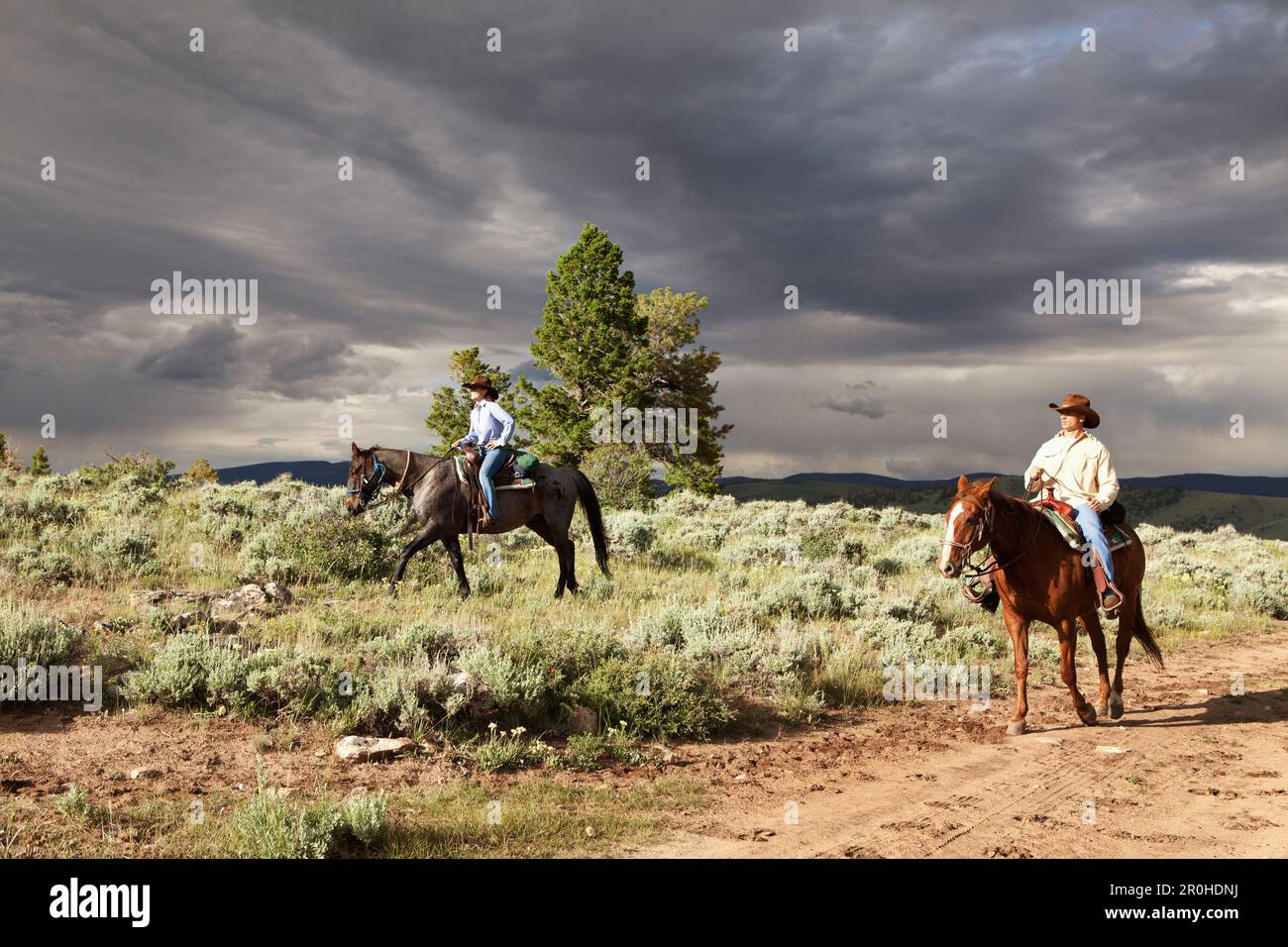 USA, Wyoming, Encampment, a man and woman ride horses under a dramatic ...