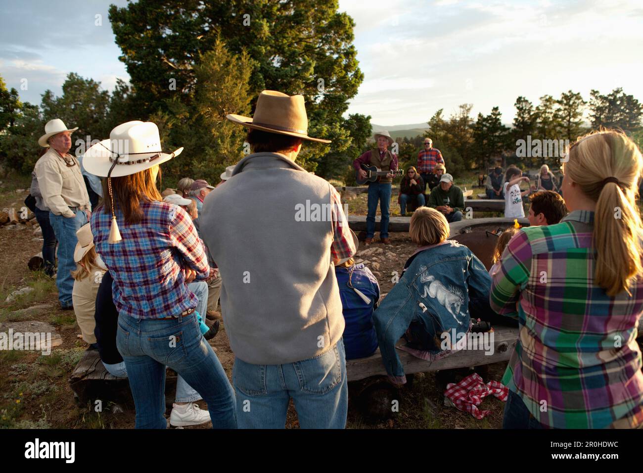 USA, Wyoming, Encampment, guests at a dude ranch sit around a campfire ...