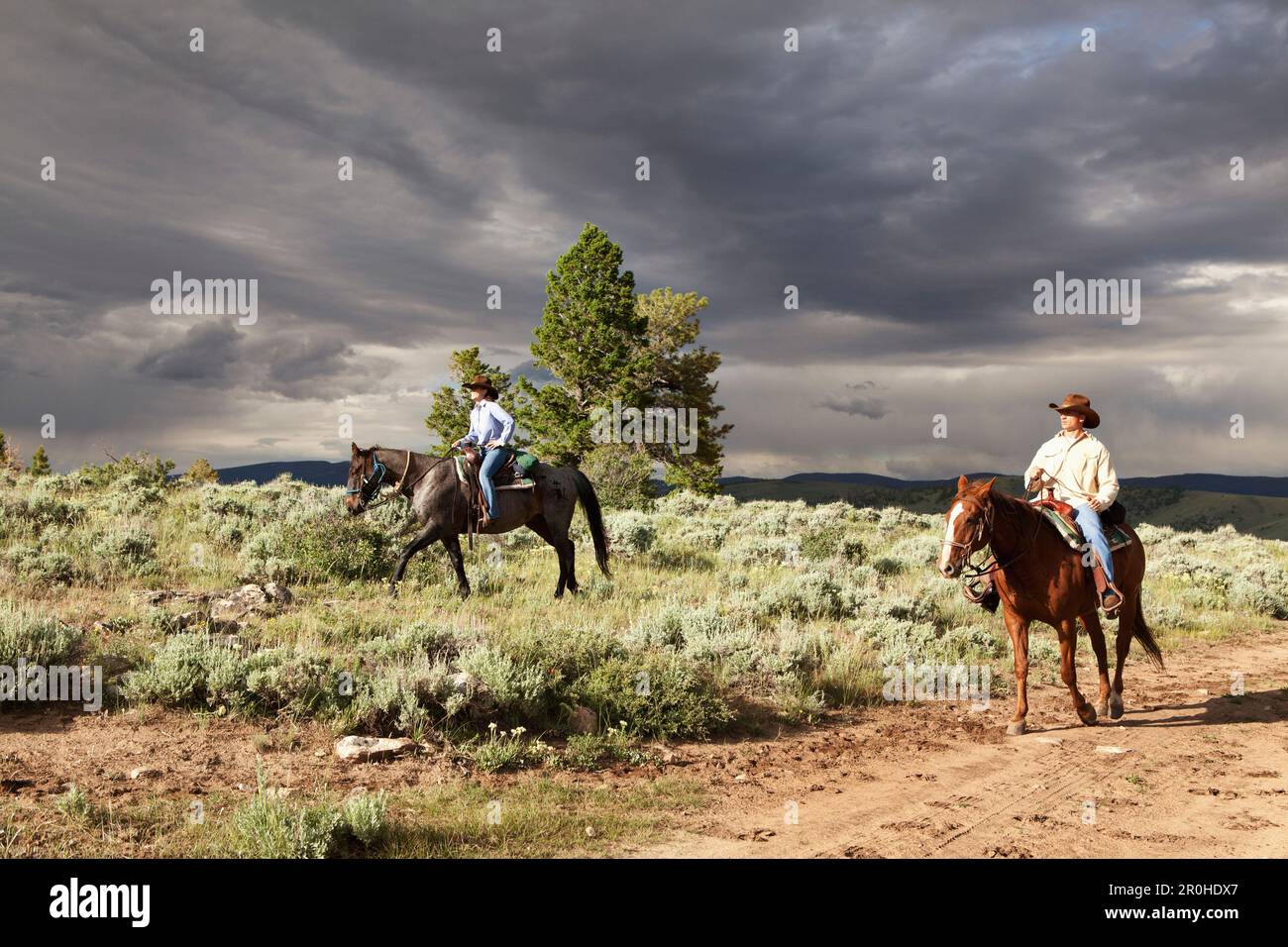 USA, Wyoming, Encampment, a man and woman ride horses under a dramatic ...