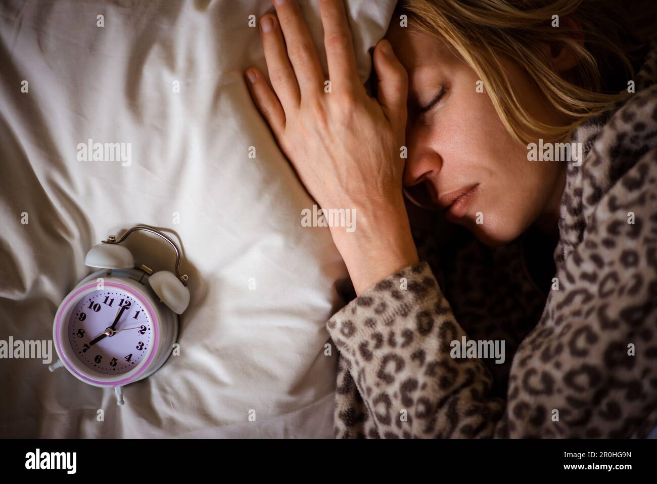 Alarm clock on the pillow and a sleeping woman. The concept of sleep ...